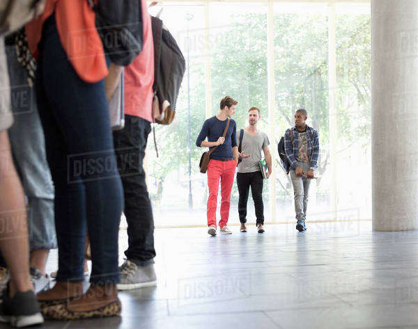Three male students walking along corridor talking with large window in ...