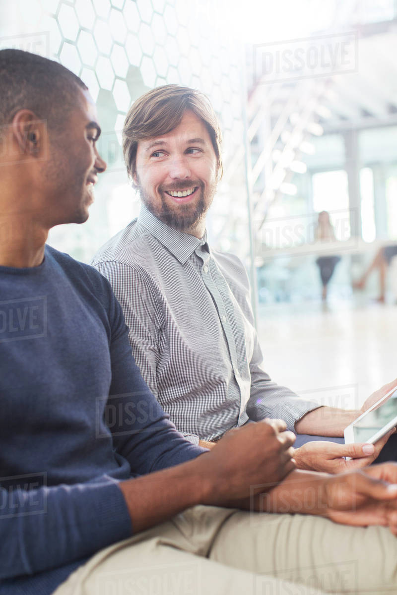 Two smiling men talking, holding digital tablet in office corridor ...
