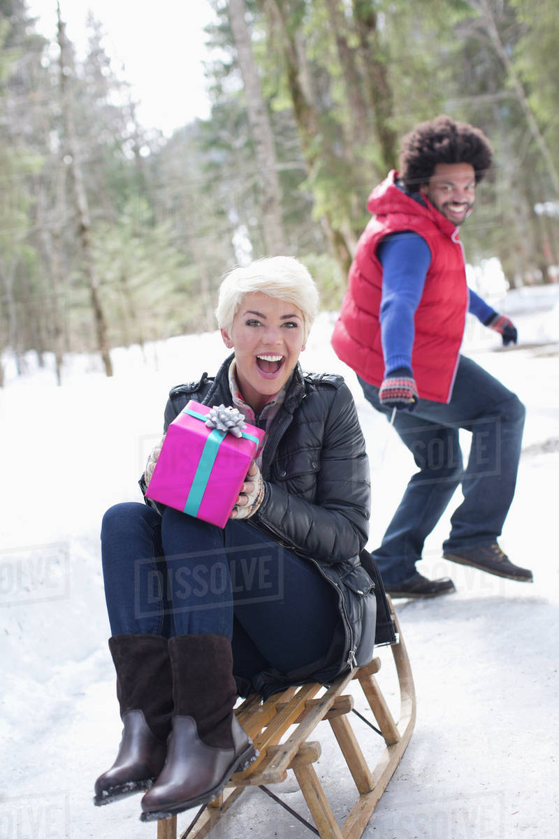 Man pulling woman with gift on sled in snow - Stock Photo - Dissolve