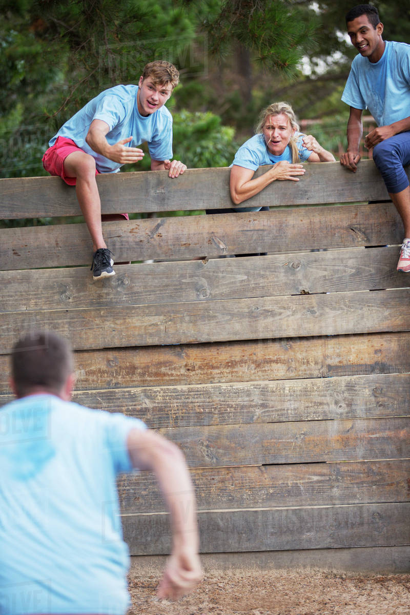 Teammates at wall cheering man on boot camp obstacle course - Royalty ...