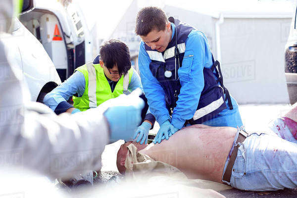 Rescue workers performing CPR on car accident victim in road - Royalty ...