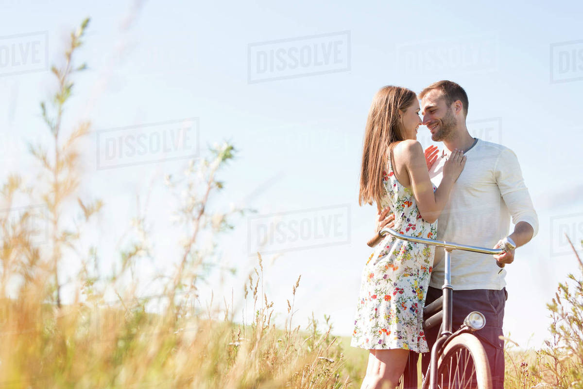 Affectionate young couple with bike hugging in sunny rural field ...