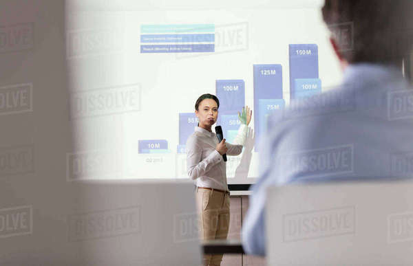 Businesswoman with microphone speaking at projection screen with bar ...