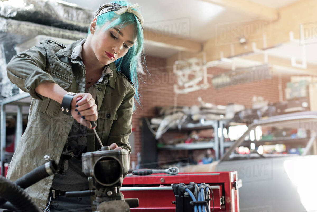 Young female mechanic with blue hair repairing part in auto repair shop ...