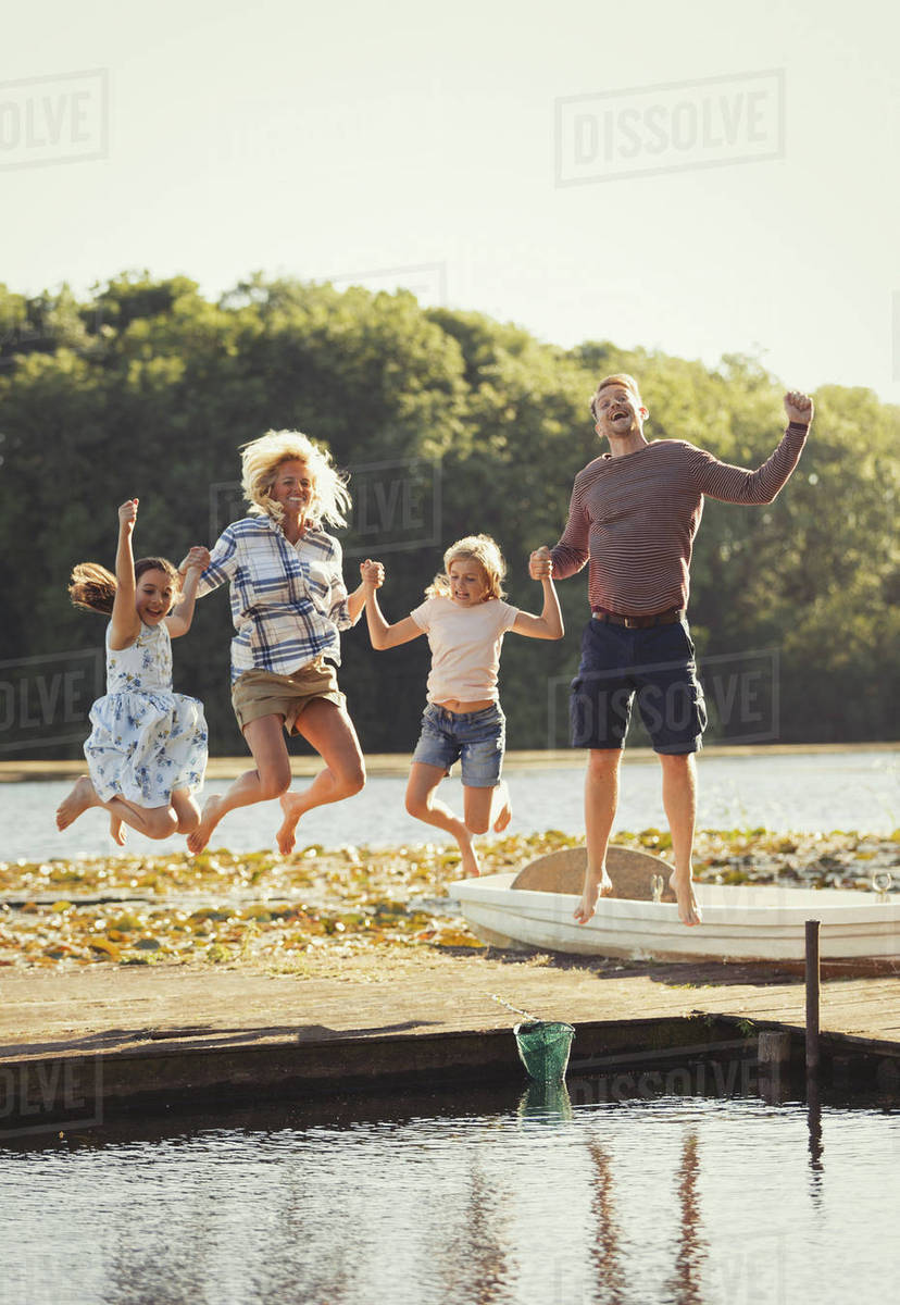 Portrait playful family jumping on sunny lake dock - Stock Photo - Dissolve