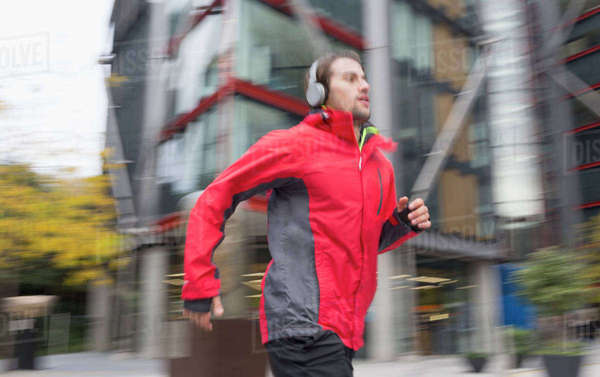Man running with headphones past urban building - Stock Photo - Dissolve