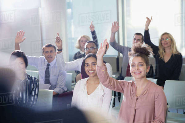 Smiling business people asking a question in conference audience ...