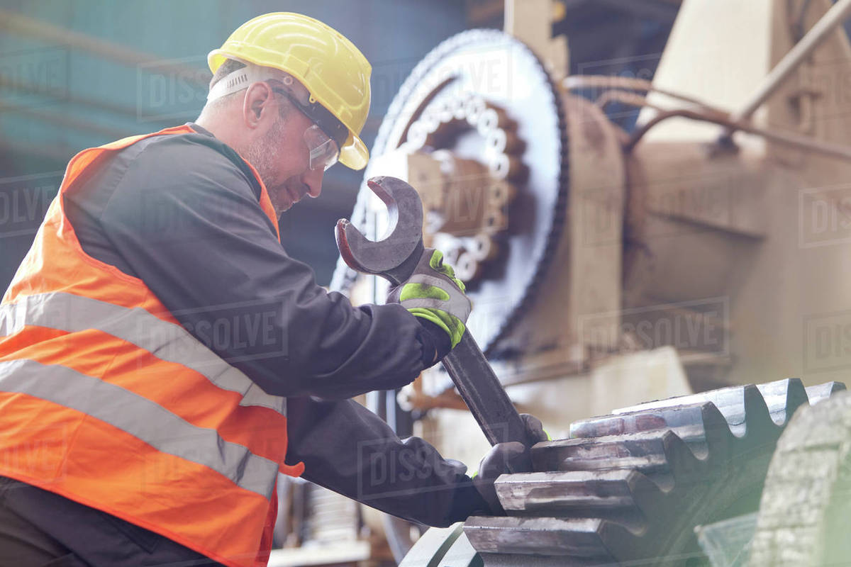 Male worker using large wrench on cog in factory - Stock Photo - Dissolve