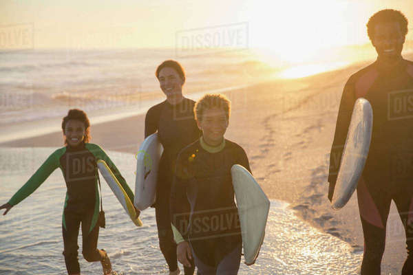 Family surfers walking with surfboards on sunny summer sunset ocean ...