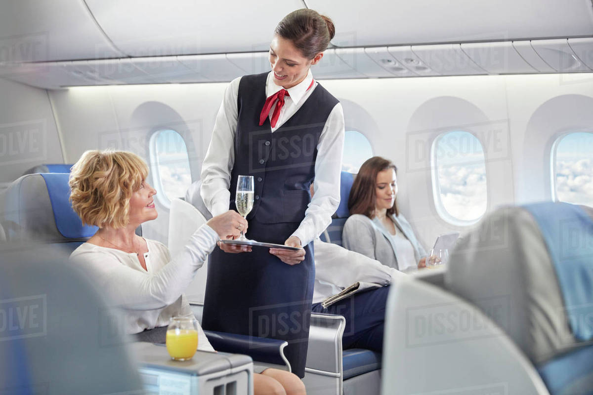 Flight attendant serving champagne to woman in first class on airplane ...
