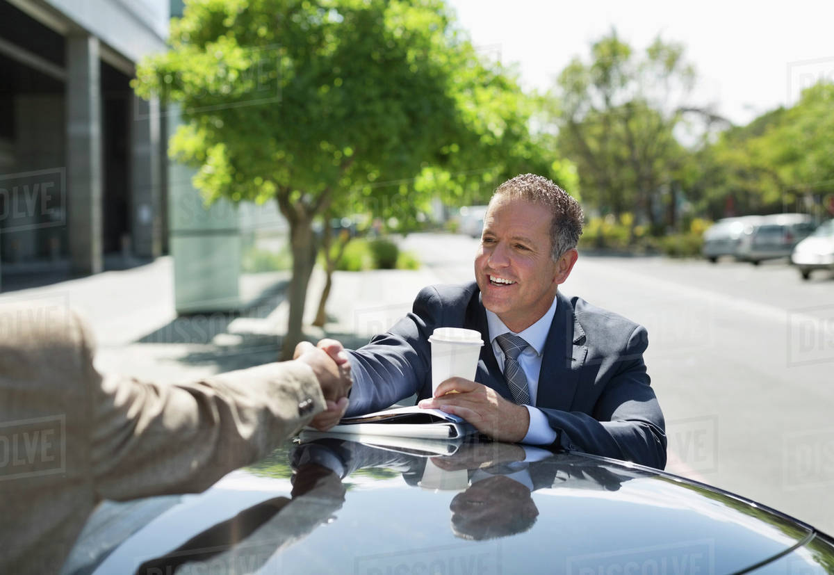 Businessmen shaking hands over car - Stock Photo - Dissolve