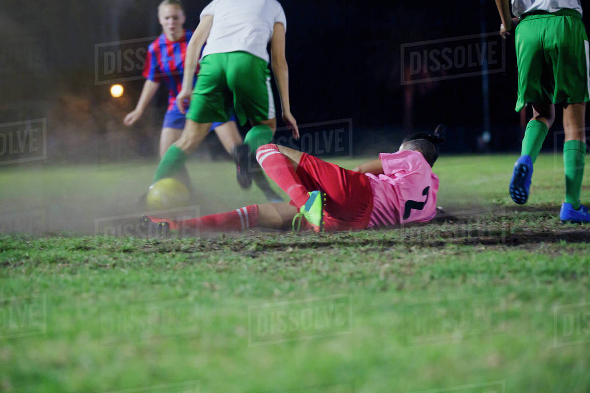 Young female soccer player falling, kicking the ball playing soccer on ...