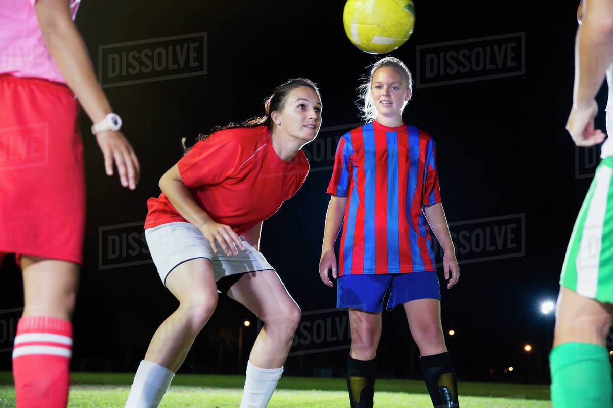 Young female soccer players practicing on field at night, heading the ...