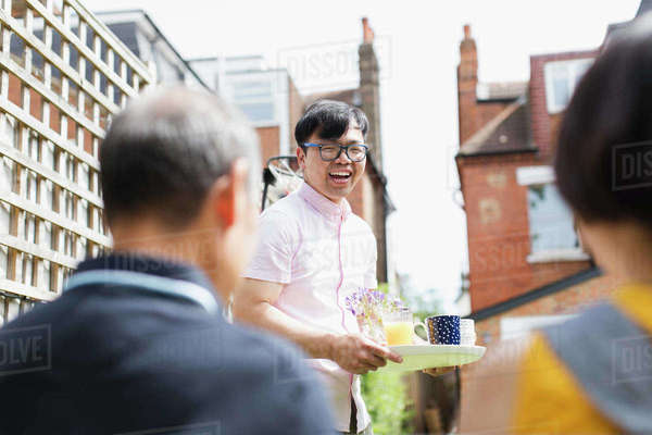 Happy man serving tea and juice to family in sunny yard - Royalty-free ...