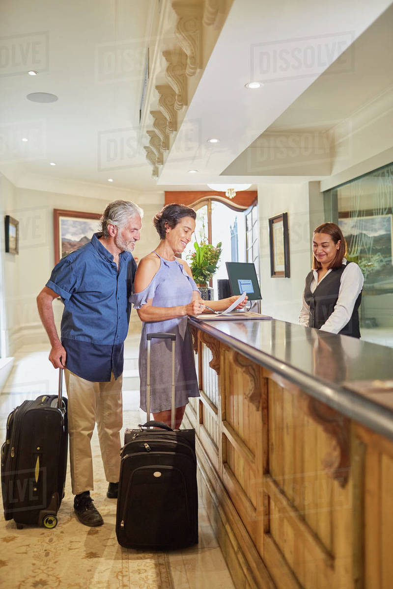 Mature couple with suitcases checking in at hotel reception - Stock ...