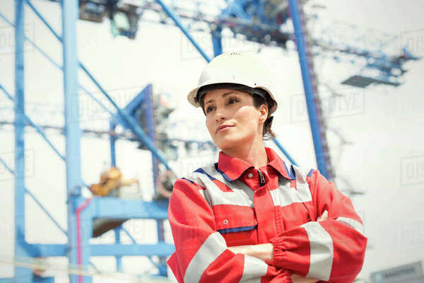 Confident female dock worker with arms crossed at shipyard - Stock ...