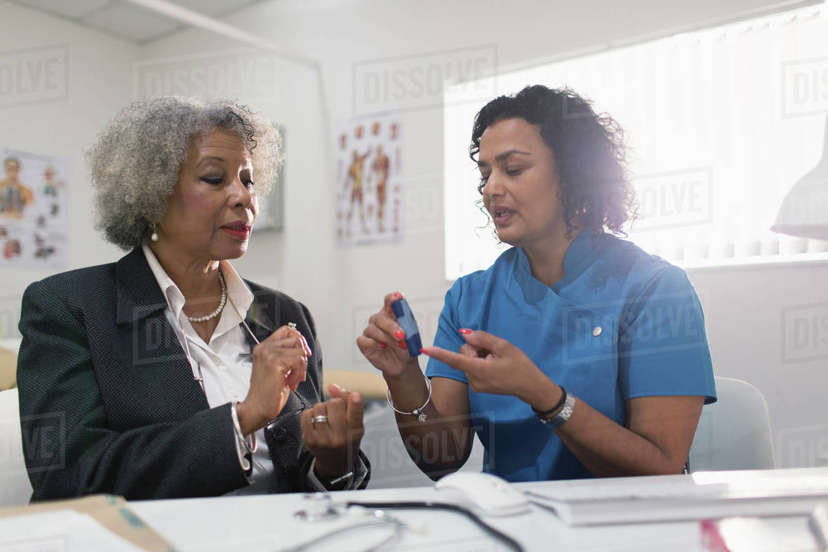 Female doctor teaching diabetic patient how to use glucometer in ...