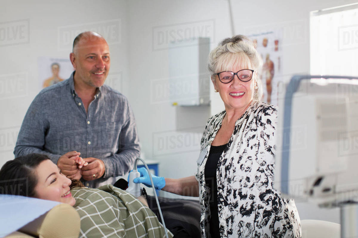 Technician performing ultrasound for happy pregnant couple in ...