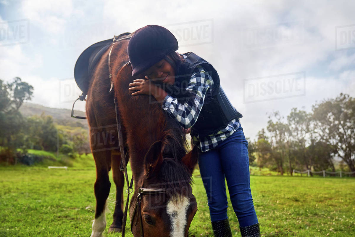 Happy girl hugging horse in rural grass paddock - Stock Photo - Dissolve