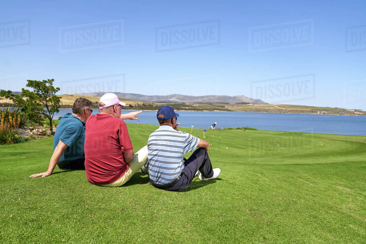 Male golfers relaxing looking at lake view from sunny golf course ...
