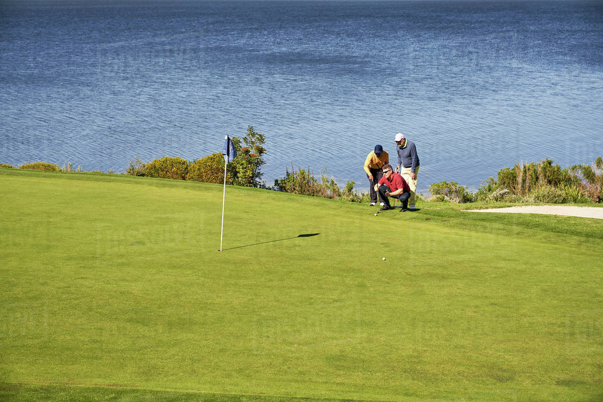 Male golfers planning putt shot at sunny lakeside golf course - Royalty ...
