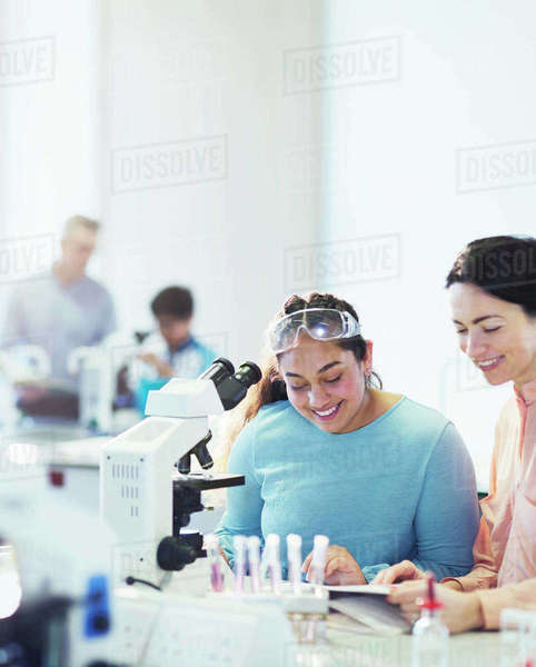 Smiling female science teacher and girl student reading textbook at ...