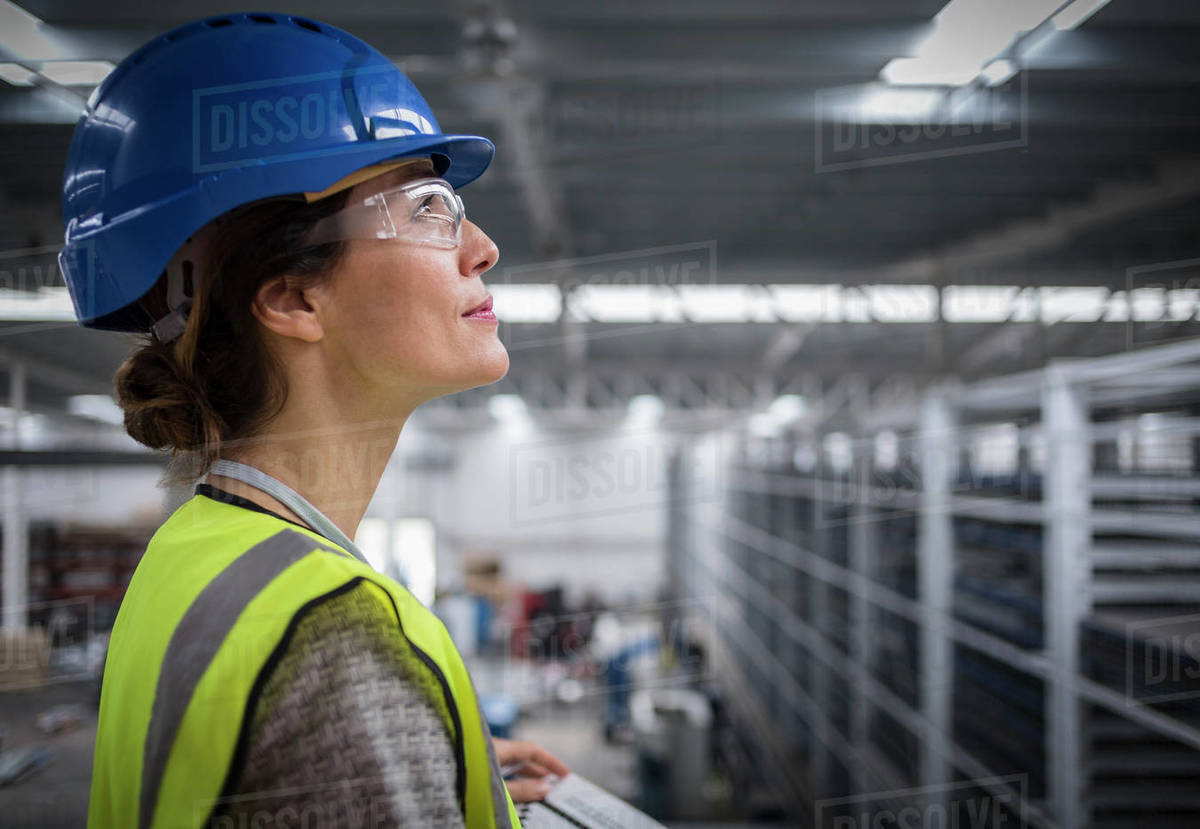 Smiling, confident female supervisor in hard-hat looking up in factory ...
