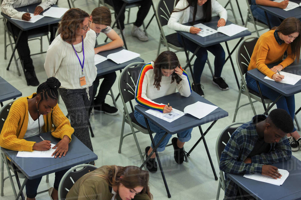 High school teacher supervising students taking exam at tables ...