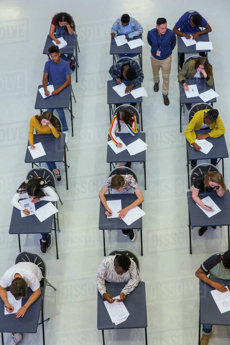 High school teacher supervising students taking exam at desks - Royalty ...