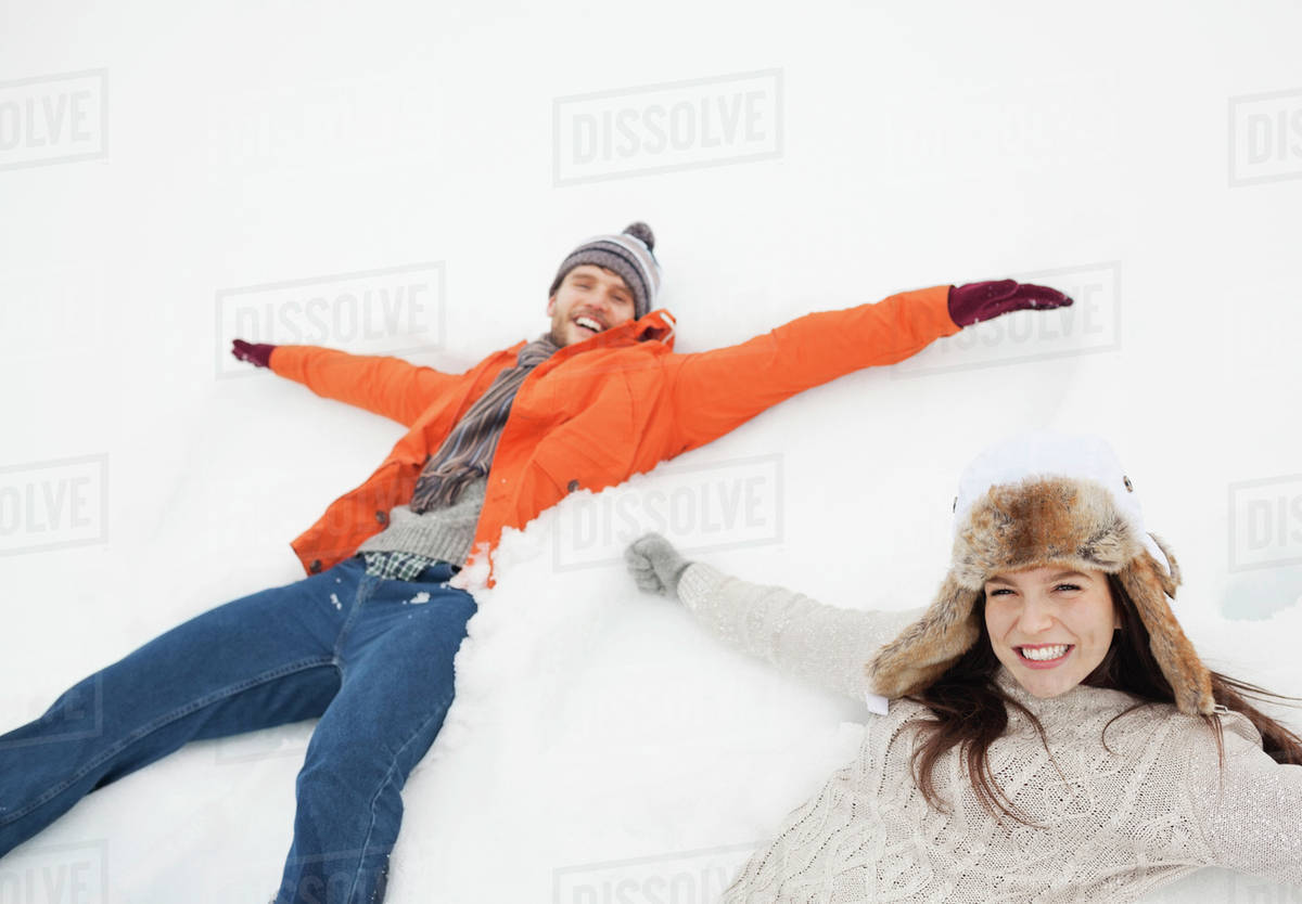 Portrait of happy couple making snow angels - Stock Photo - Dissolve