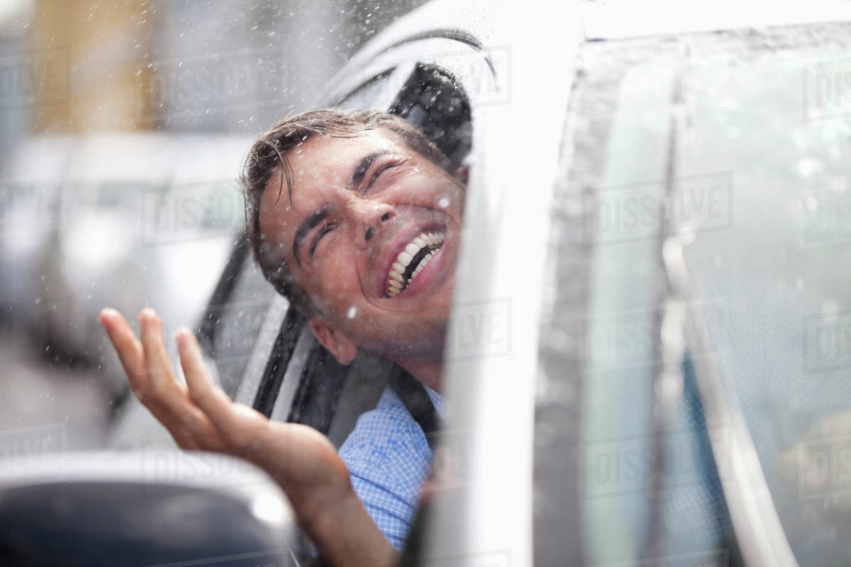 Enthusiastic man in car looking out window at rain - Stock Photo - Dissolve