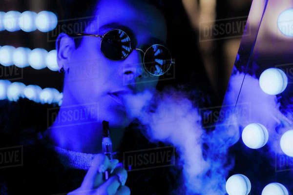 Portrait cool young man in sunglasses vaping in dark neon. nightclub ...