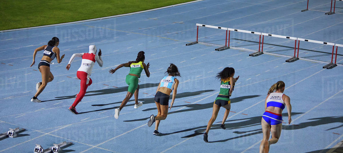 Female track and field athletes racing toward hurdles in competition ...