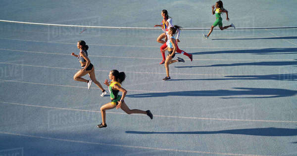 Female track and field athletes running in competition on blue track ...