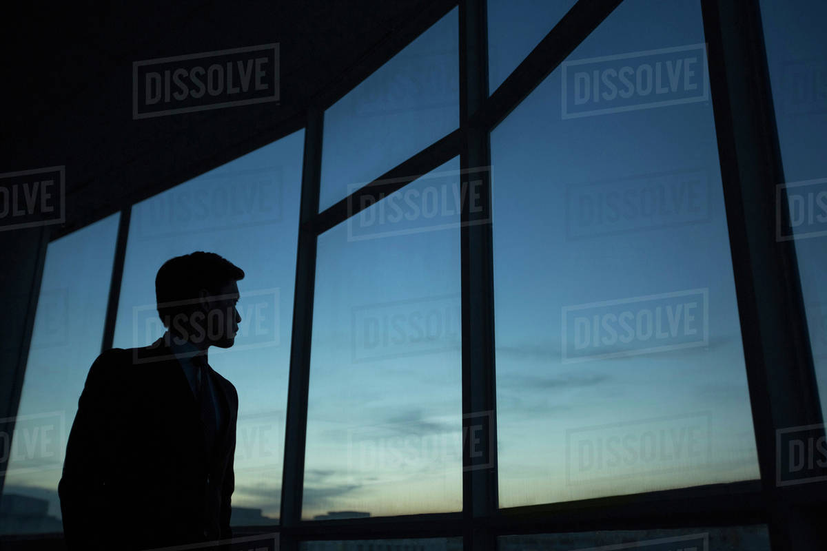 Businessman standing by window at dusk - Stock Photo - Dissolve