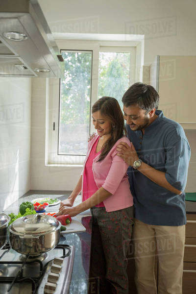 Man standing behind woman in kitchen while she cooks - Royalty-free ...
