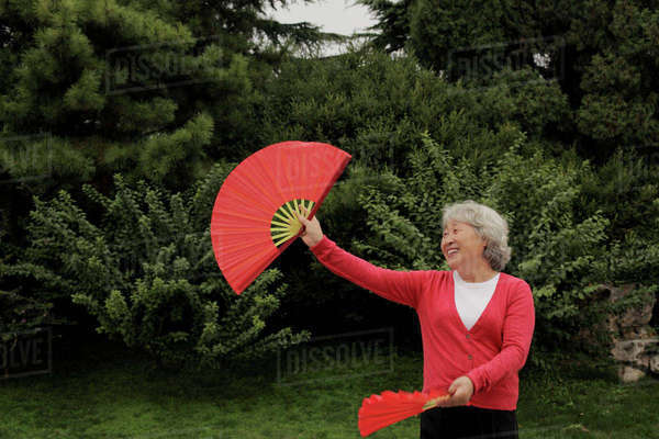 Older woman dancing with fan dance outdoors - Stock Photo - Dissolve