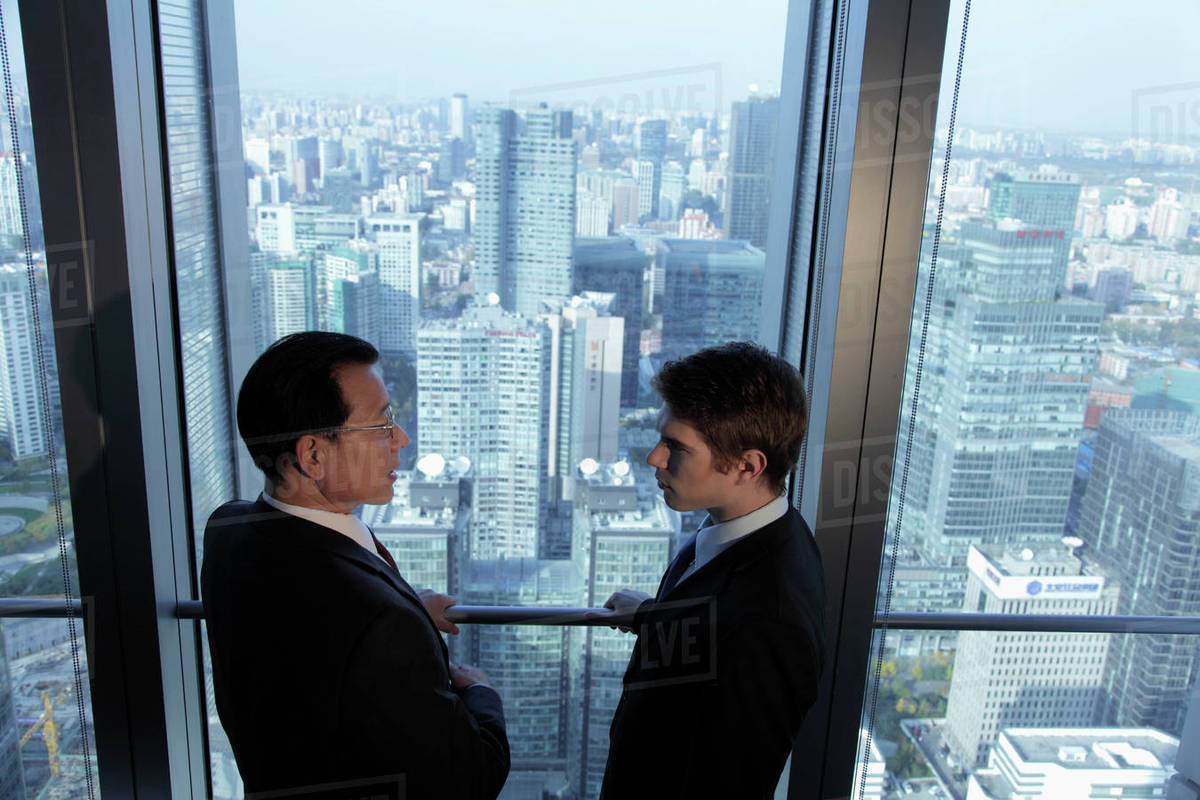 Two men talking in front of window with a view of the city of Beijing ...