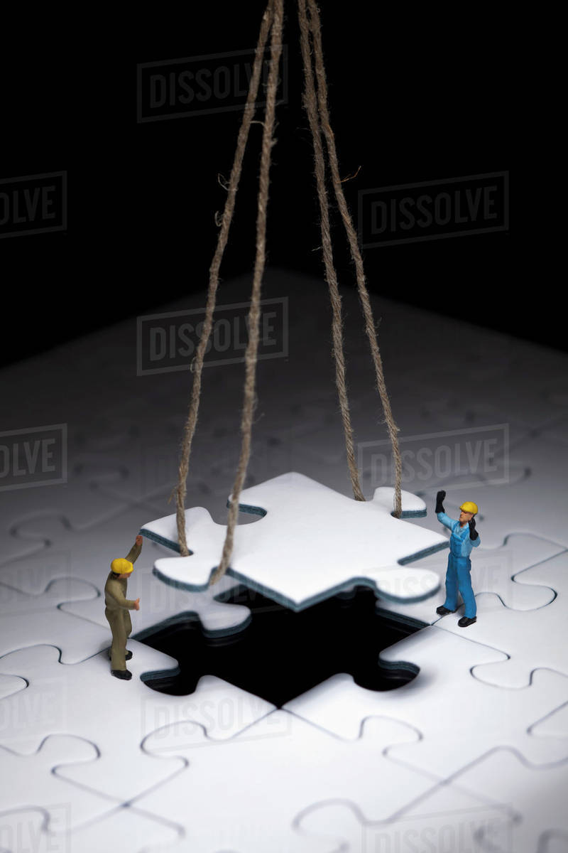 Miniature workmen guiding a hanging puzzle piece into place - Royalty ...