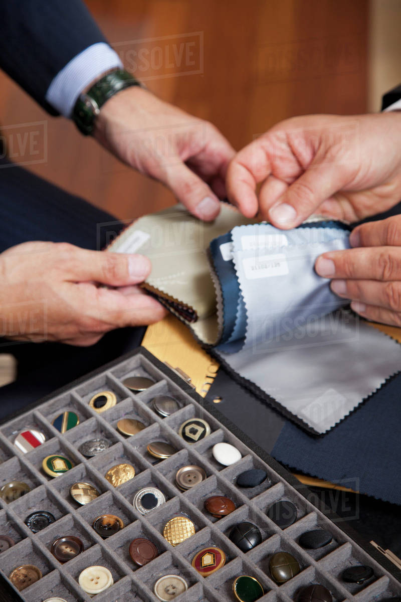 Detail of a tray of buttons and two men looking at fabric samples ...