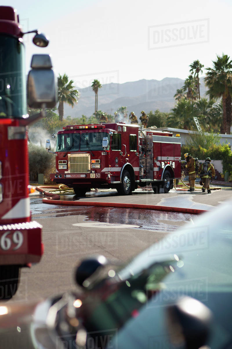 A fire truck and firefighters on a suburban street next to a burning ...