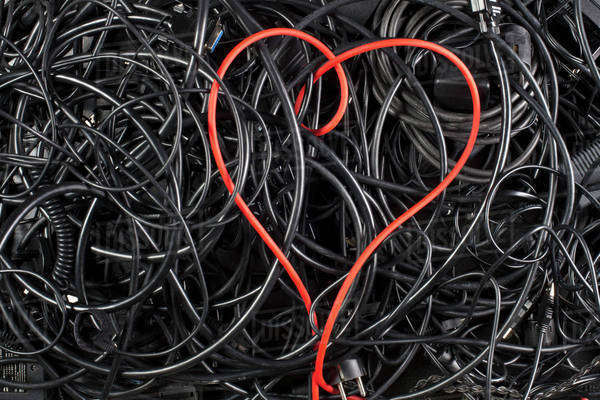 A red cord in a heart shape amongst tangled black cables and cords ...