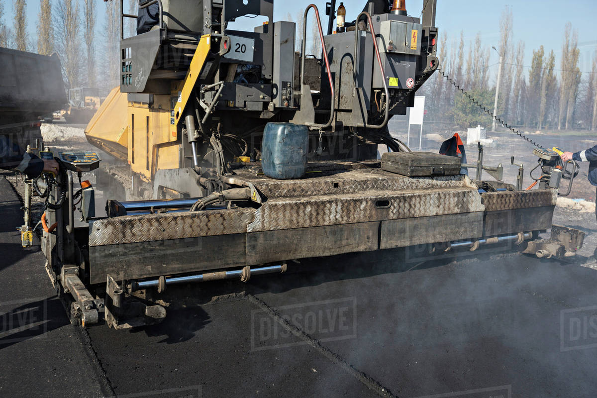 Manual workers controlling large road surfacing machine being trailed ...