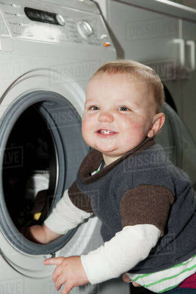A baby boy standing next to a washing machine - Stock Photo - Dissolve