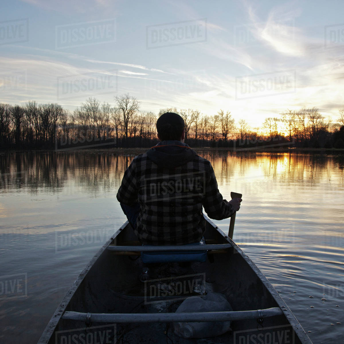 A man in a canoe on a lake at sunset, rear view - Stock Photo - Dissolve