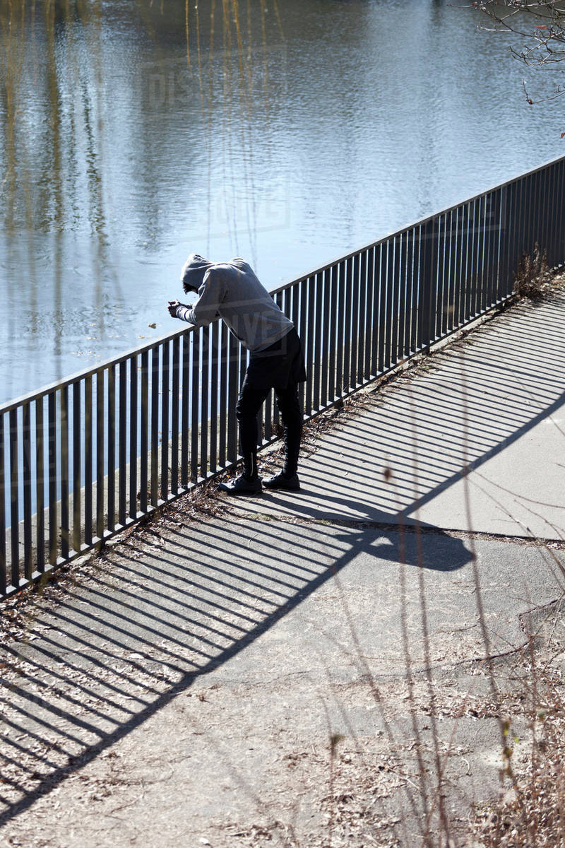 A young man leaning against a railing looking down at a river - Royalty ...