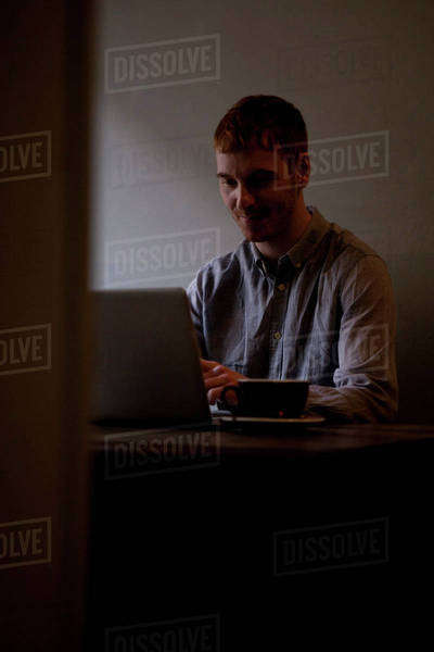 A man sitting at a table in a cafe using a laptop - Stock Photo - Dissolve