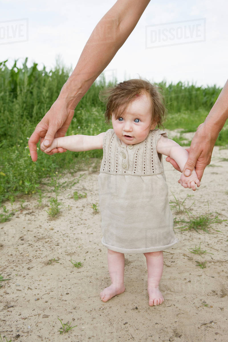 Father helping baby girl to walk - Stock Photo - Dissolve
