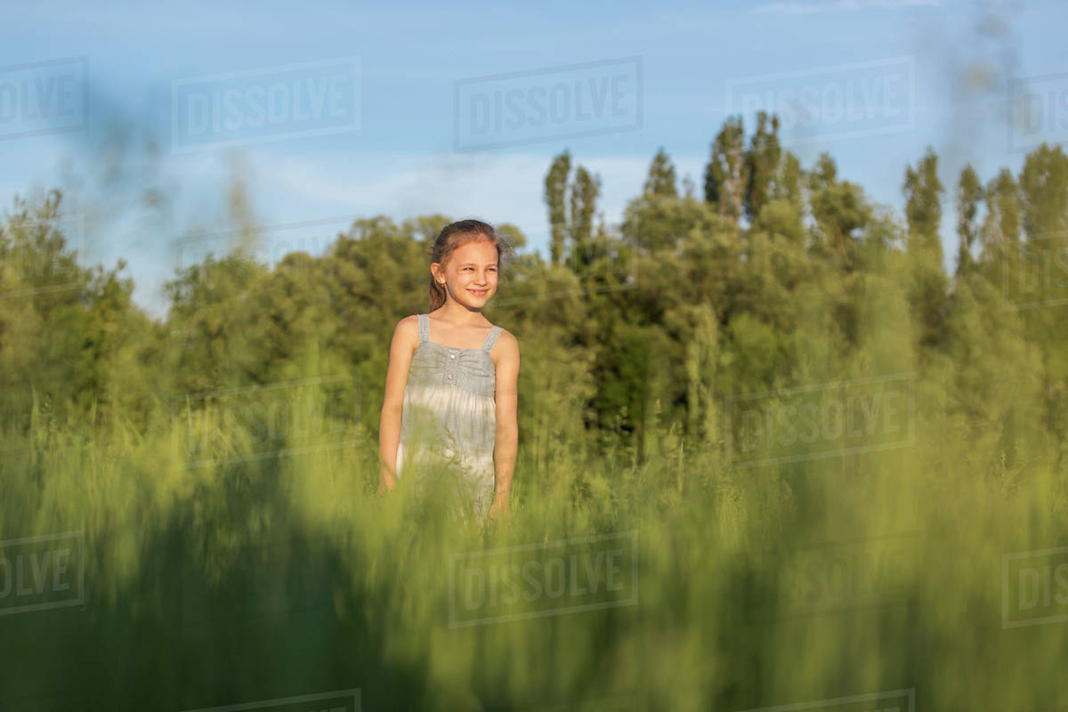A young cheerful girl standing in a field looking at the view - Royalty ...