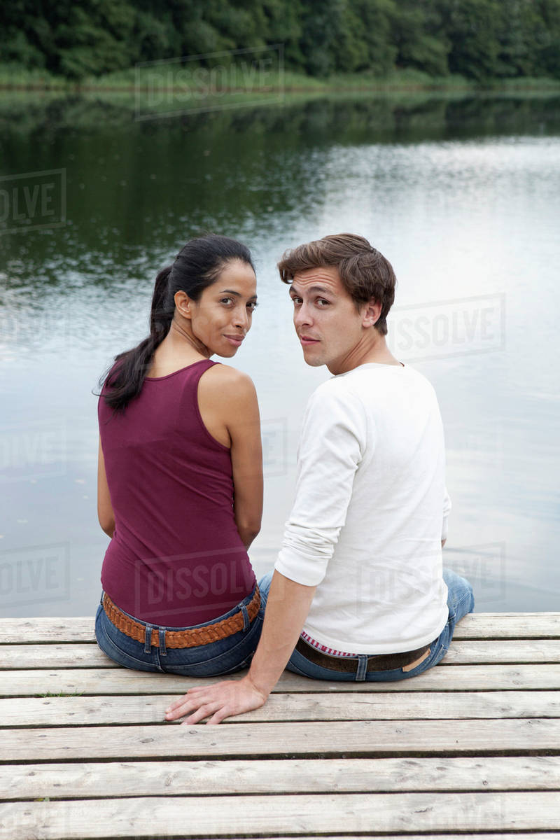 Young couple sitting on pier, looking over shoulders - Royalty-free ...